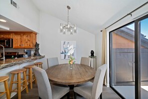 Uma mesa de jantar redonda de madeira com banquetas de bar, um lustre e um quadro na parede.