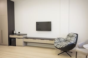 Quarto moderno e minimalista com um banco embutido, uma cadeira preta com almofada estampada e uma TV de tela plana fixada na parede.