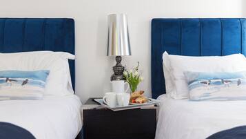 Quarto de hotel com duas camas, uma mesa de cabeceira com abajur, um tabuleiro com itens de café da manhã e um vaso com flores.
