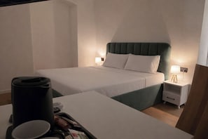Quarto de hotel com cama, mesas de cabeceira, cafeteira e uma bandeja com lanches.