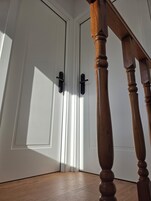 Canto de um quarto com piso de madeira e portas brancas com puxadores pretos.