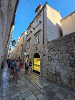 Uma rua estreita com edifícios de pedra, uma loja com vitrine e pedestres.