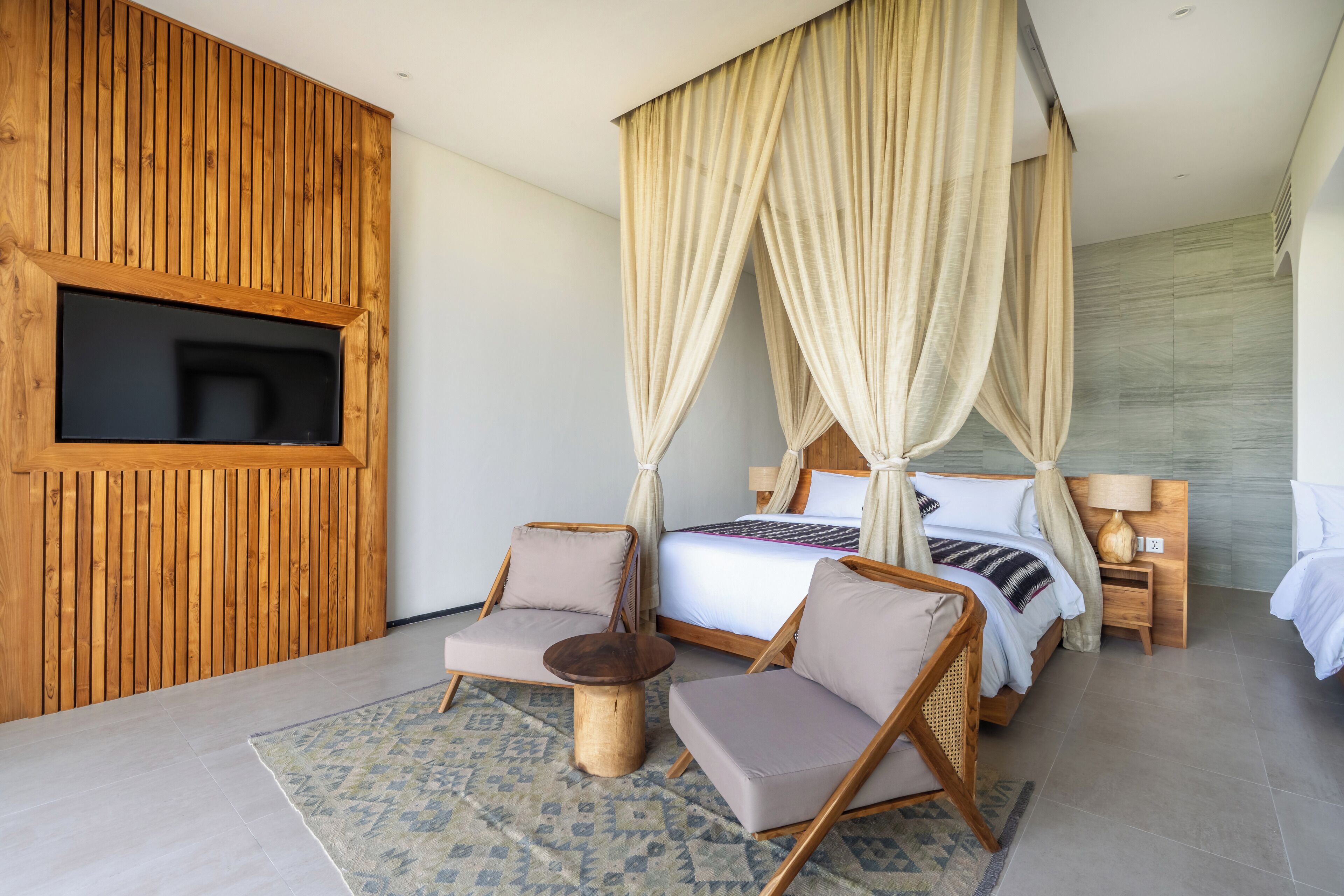 Quarto moderno com parede de painéis de madeira, uma cama com dossel, duas cadeiras, uma mesinha e um abajur.
