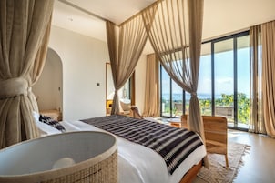 Quarto com uma cama grande, vista para o mar e uma varanda com uma cadeira.