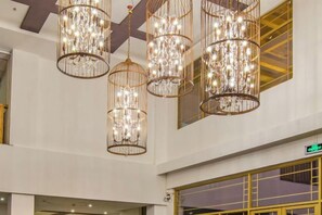 Um candelabro com vários níveis e luzes, pendurado em um amplo espaço interior com tetos altos e grandes janelas.