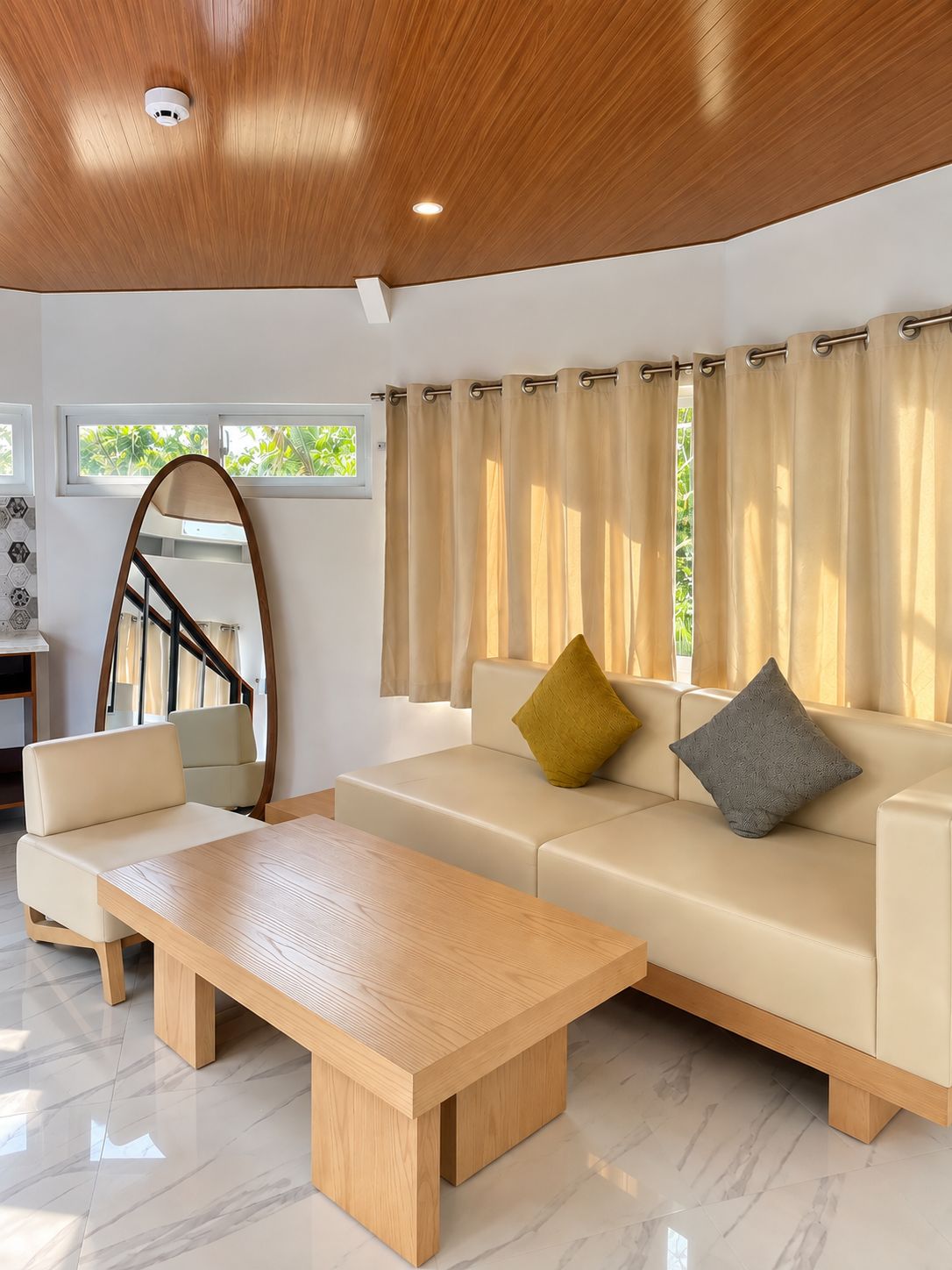 Uma sala de estar moderna com teto de madeira, sofá bege com almofadas, mesa de centro de madeira e um espelho grande.