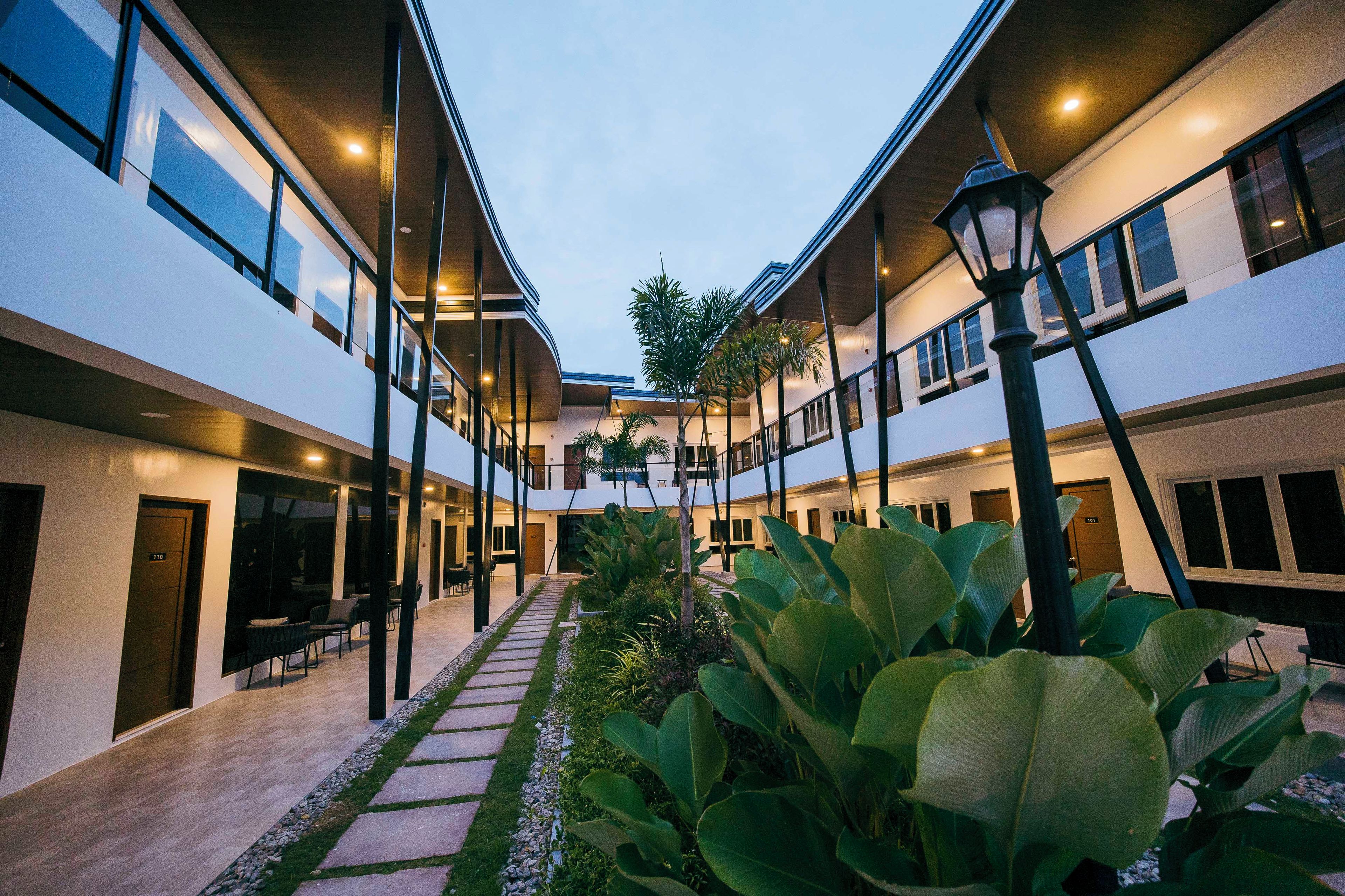 Um pátio de hotel com um caminho central, área de estar ao ar livre e várias varandas.