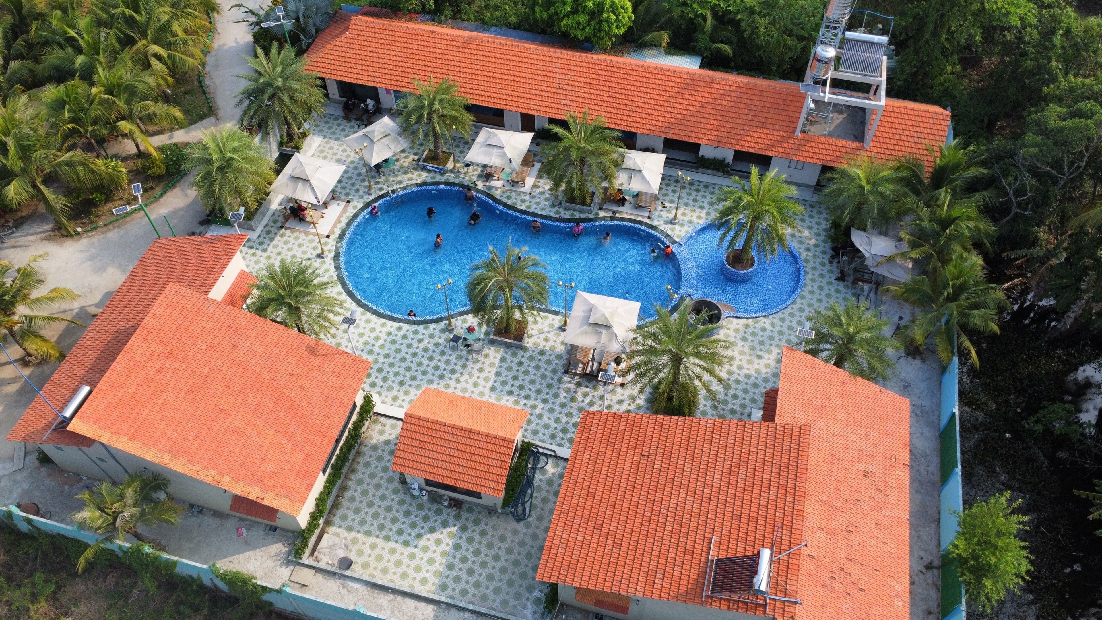 An aerial view of a resort with a swimming pool, palm trees, and a tiled roof.