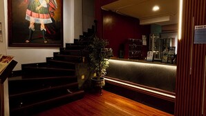 Um saguão de hotel com uma escadaria, uma mesa de recepção e uma pintura grande na parede.