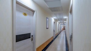 Um corredor longo e estreito, com portas em ambos os lados, piso de azulejos e rodapé de madeira.