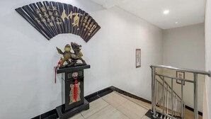 Um corredor com um leque decorativo, uma estátua e um corrimão de escada.