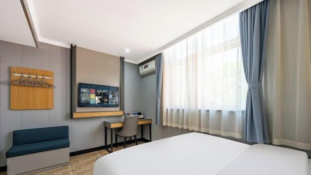 Quarto de hotel com uma cama grande, uma escrivaninha, uma cadeira, um sofá e uma janela ampla com cortinas.