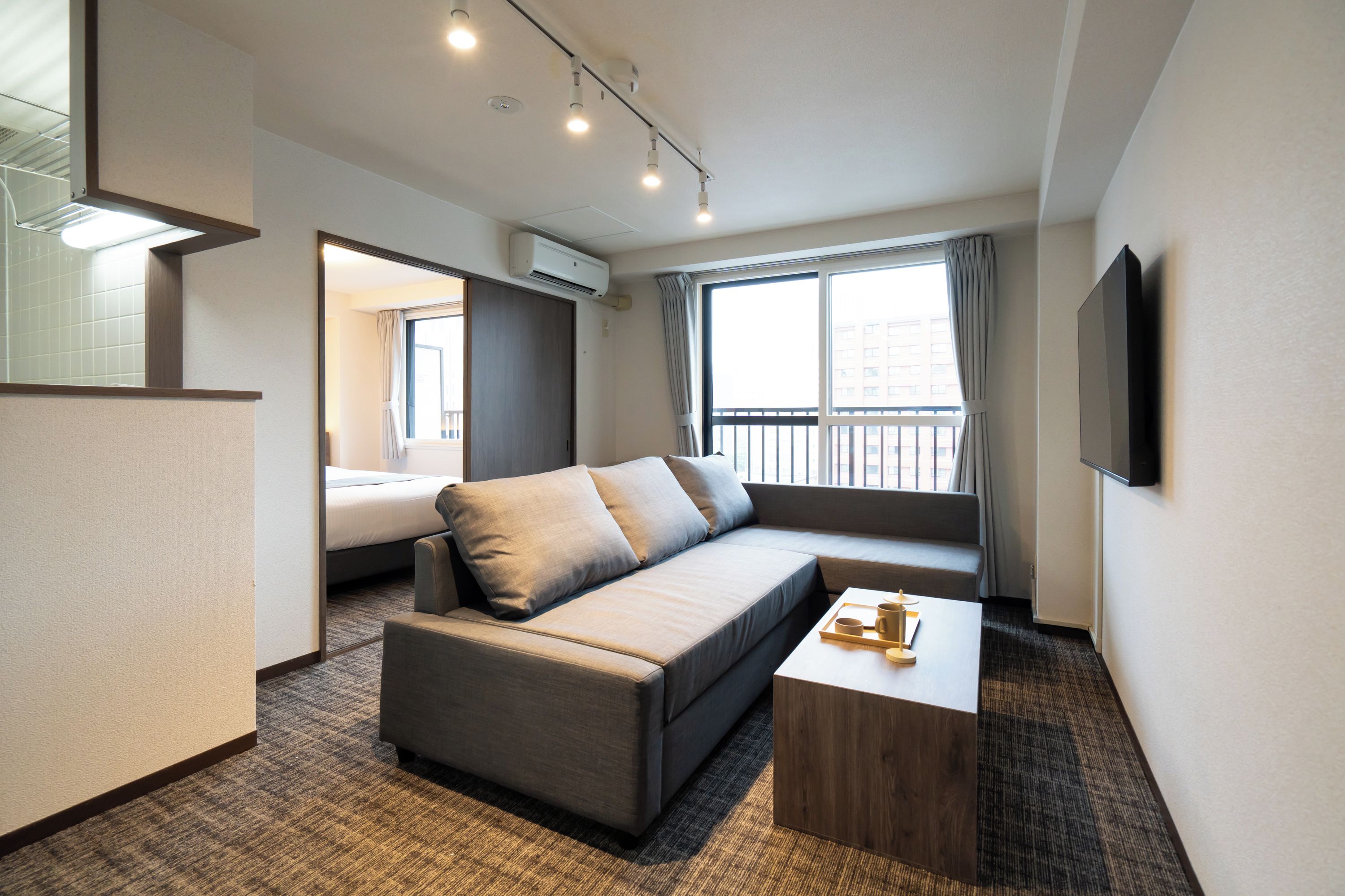 Quarto de hotel moderno com sofá, mesinha, TV de tela plana e janela com vista para a cidade.