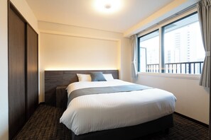 Quarto de hotel com uma cama grande, mesa de cabeceira, cabeceira, janela com cortinas e vista para edifícios.