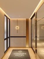 Um hall de hotel com design moderno, com balcão de recepção, divisória de vidro e tapete de entrada com o nome do hotel.