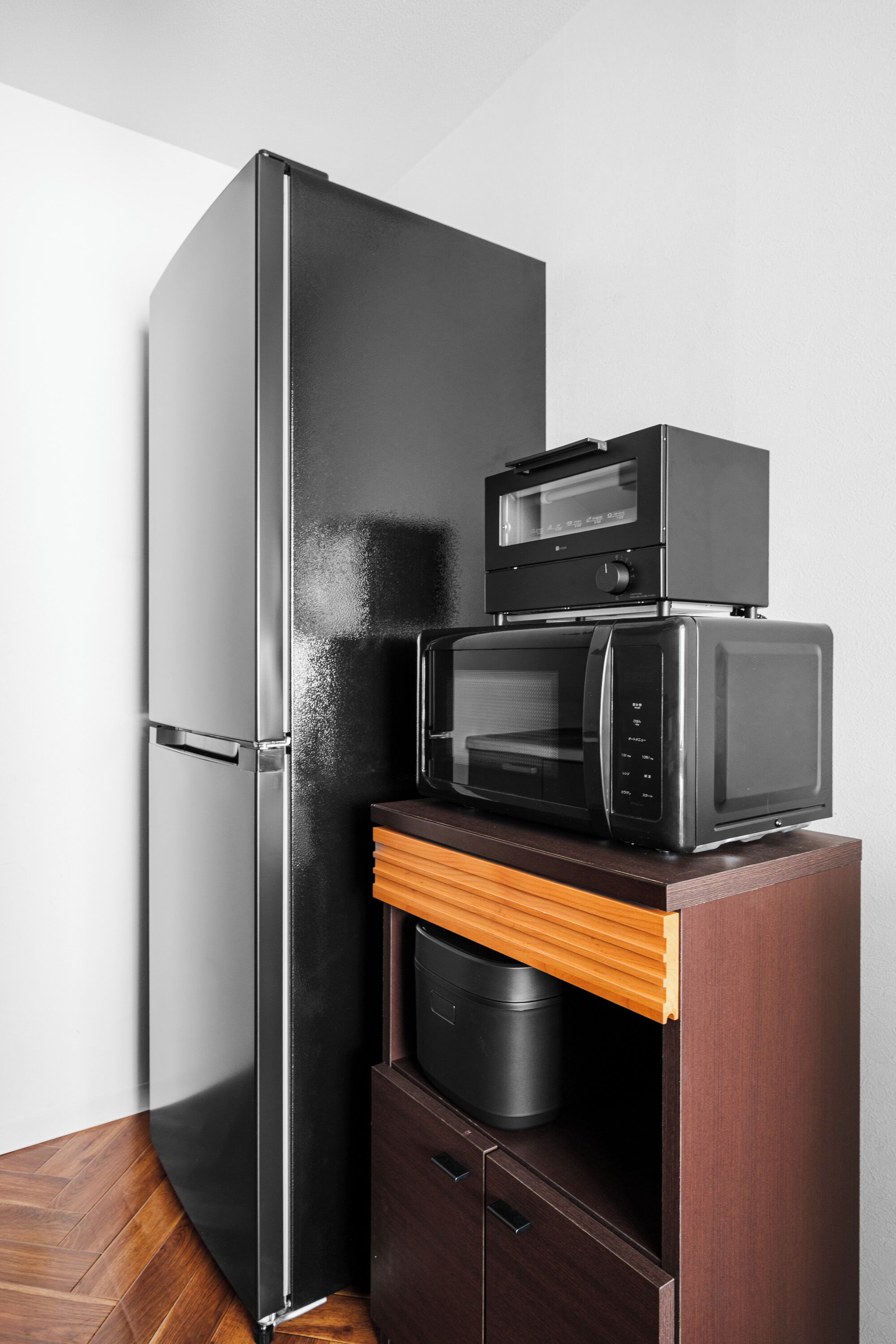 Uma cozinha compacta com geladeira preta, micro-ondas e armário de madeira abaixo.