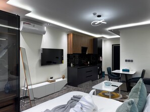 Uma sala de estar moderna com televisão de tela plana, área de refeições e cozinha com armários escuros.