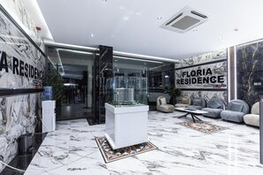 Um lobby moderno com piso de mármore, um balcão de recepção, uma vitrine de vidro e uma área de estar com sofás.
