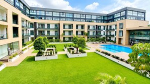 Um edifício moderno com um pátio central, piscina e um gramado bem cuidado.