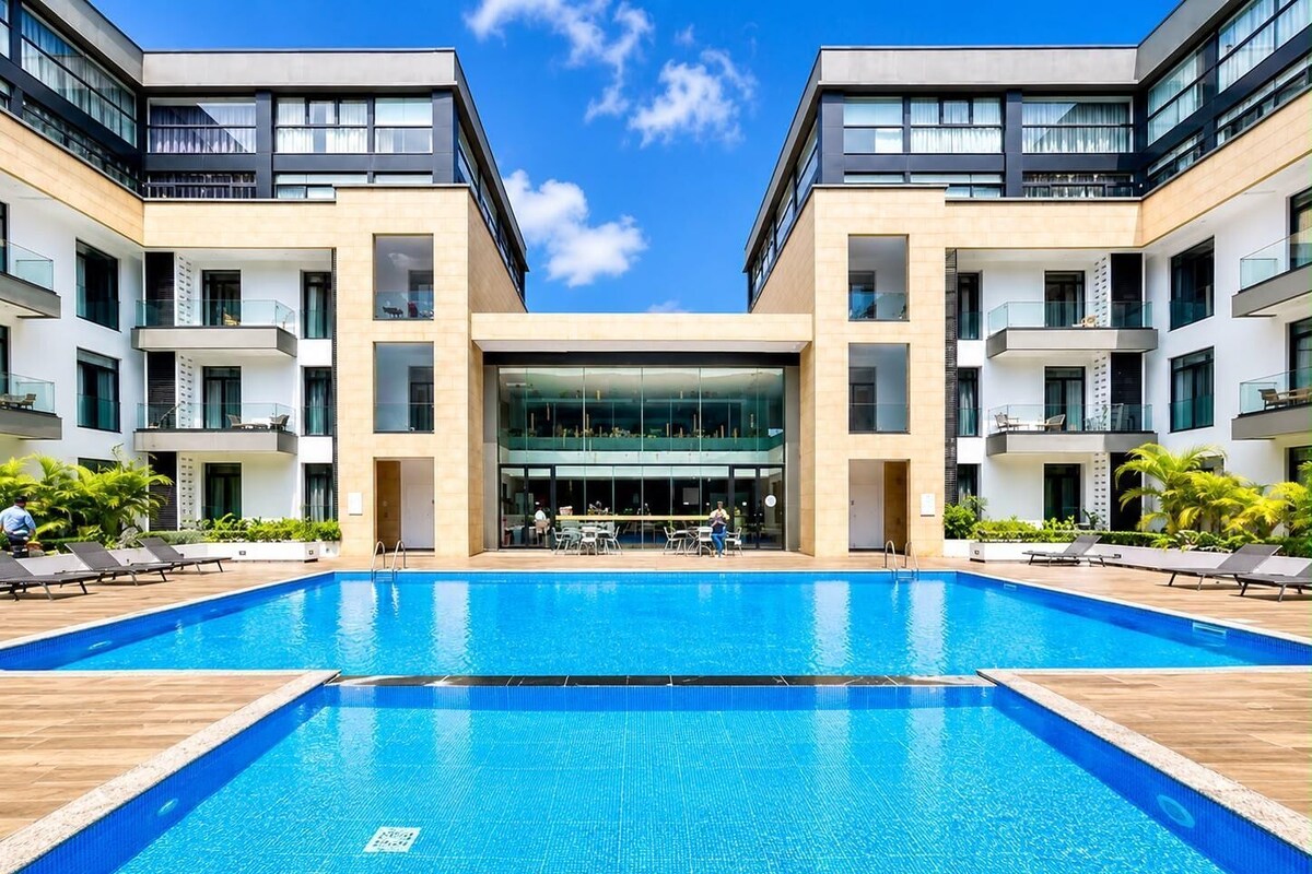Um hotel moderno com piscina central, várias varandas e fachada de vidro.
