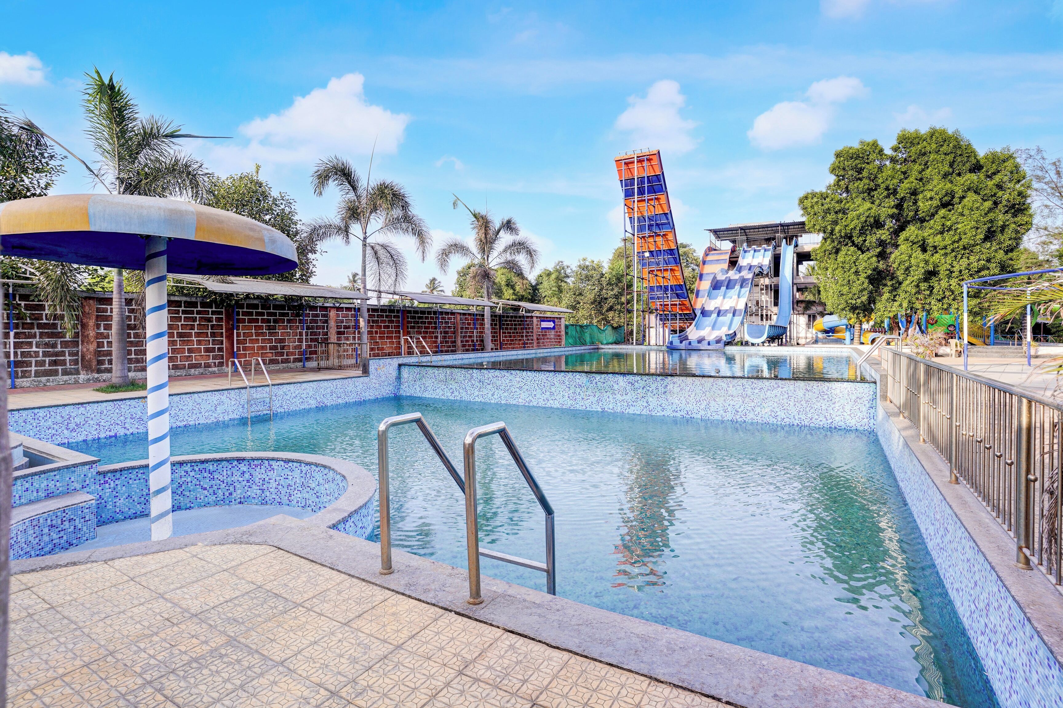 Piscina com borda azulejada, prancha de mergulho e toboáguas ao fundo.