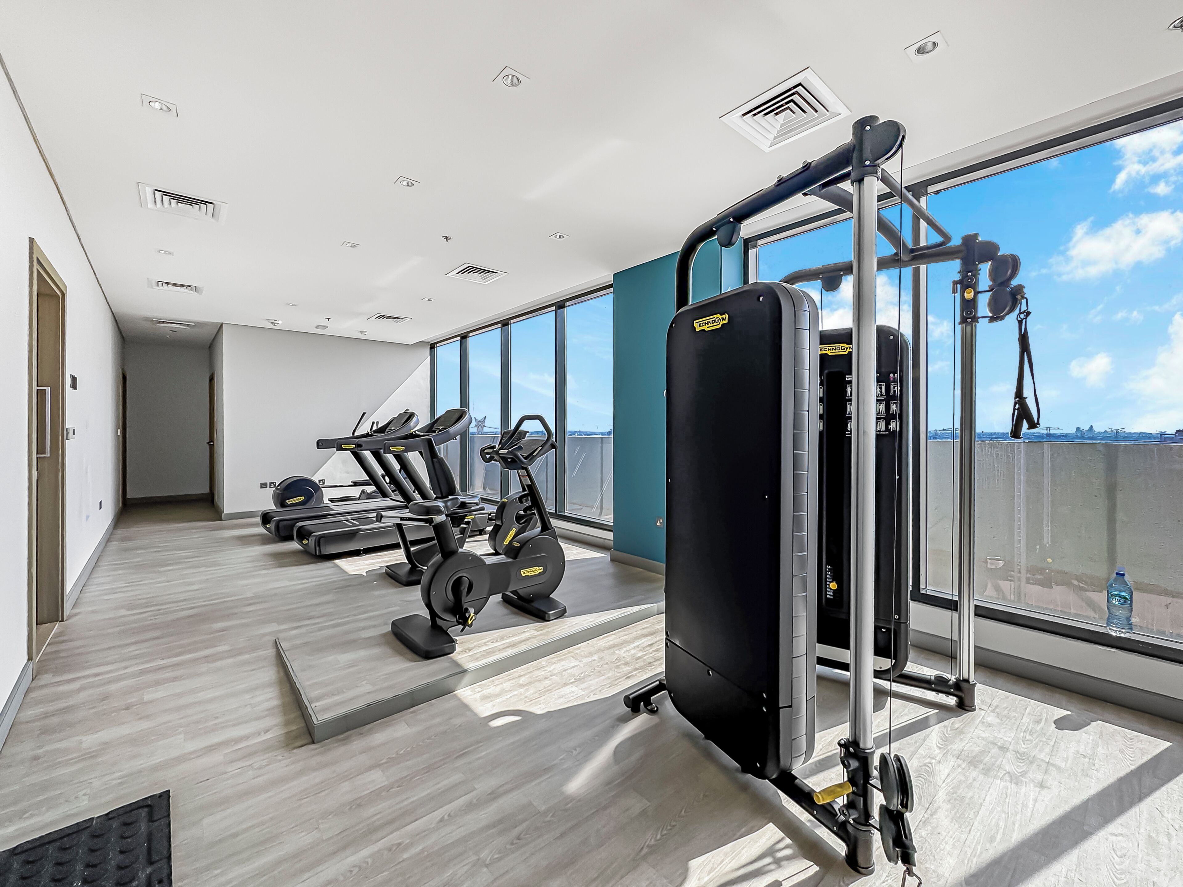 Academia com máquinas de cardio, equipamentos de musculação e amplas janelas com vista.