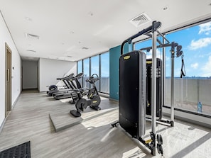 Academia com máquinas de cardio, equipamentos de musculação e amplas janelas com vista.