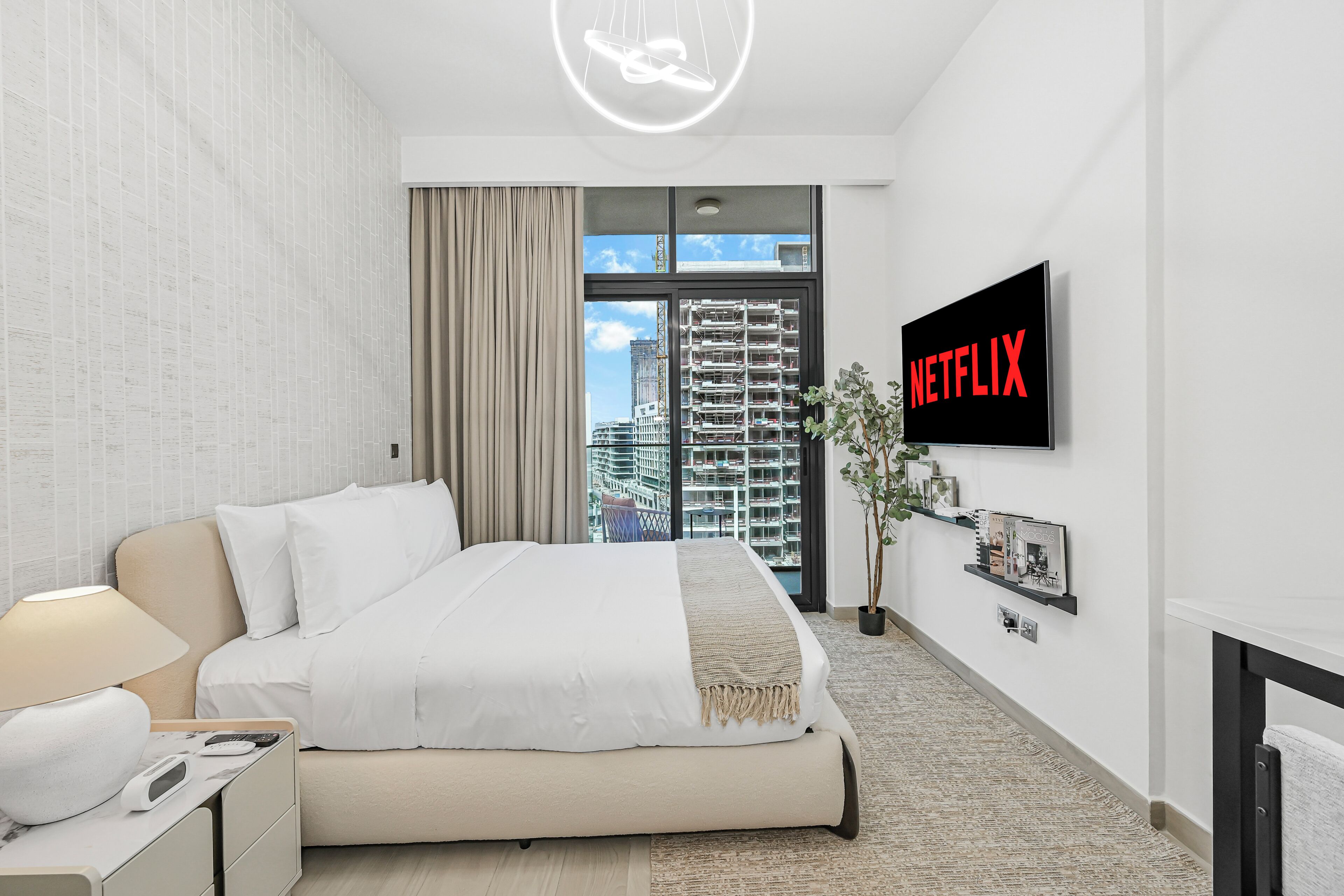 Quarto de hotel moderno com cama, mesa de cabeceira, abajur e televisão exibindo o logotipo da Netflix.