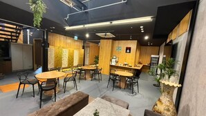 Um interior moderno com mesas e cadeiras redondas, uma área de estar com um banco acolchoado, e um espaço de bar com painéis de madeira e um balcão.