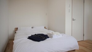 Quarto individual com uma cama, chão de madeira, roupa de cama branca e porta fechada.