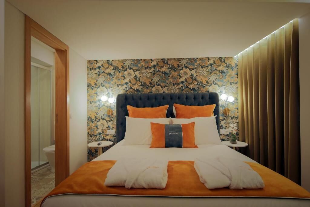 Quarto de hotel com uma cama grande, papel de parede floral e mesa de cabeceira com abajur.