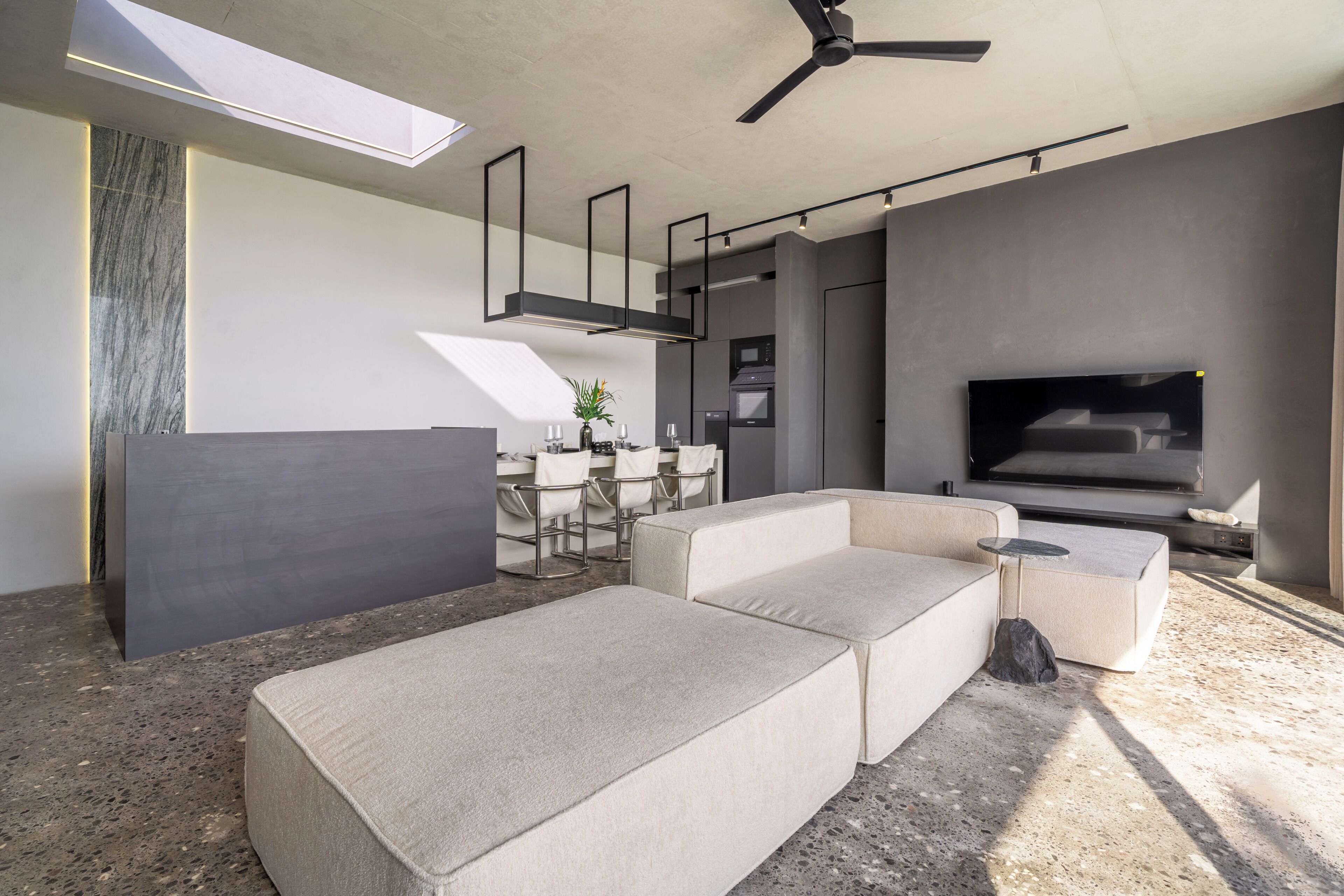 Uma sala de estar moderna com um sofá seccional, uma televisão de tela plana e um ventilador de teto.
