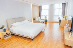 Quarto de hotel com uma cama grande, uma escrivaninha, uma cadeira, uma mesinha e uma televisão.