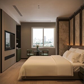 Quarto de hotel com uma cama grande, televisão, área de jantar com cadeiras e janela com vista para a cidade.