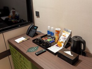 Bancada de recepção de hotel com telefone, controles remotos, cardápio, garrafa de água, sachê de sal e máquina de café.