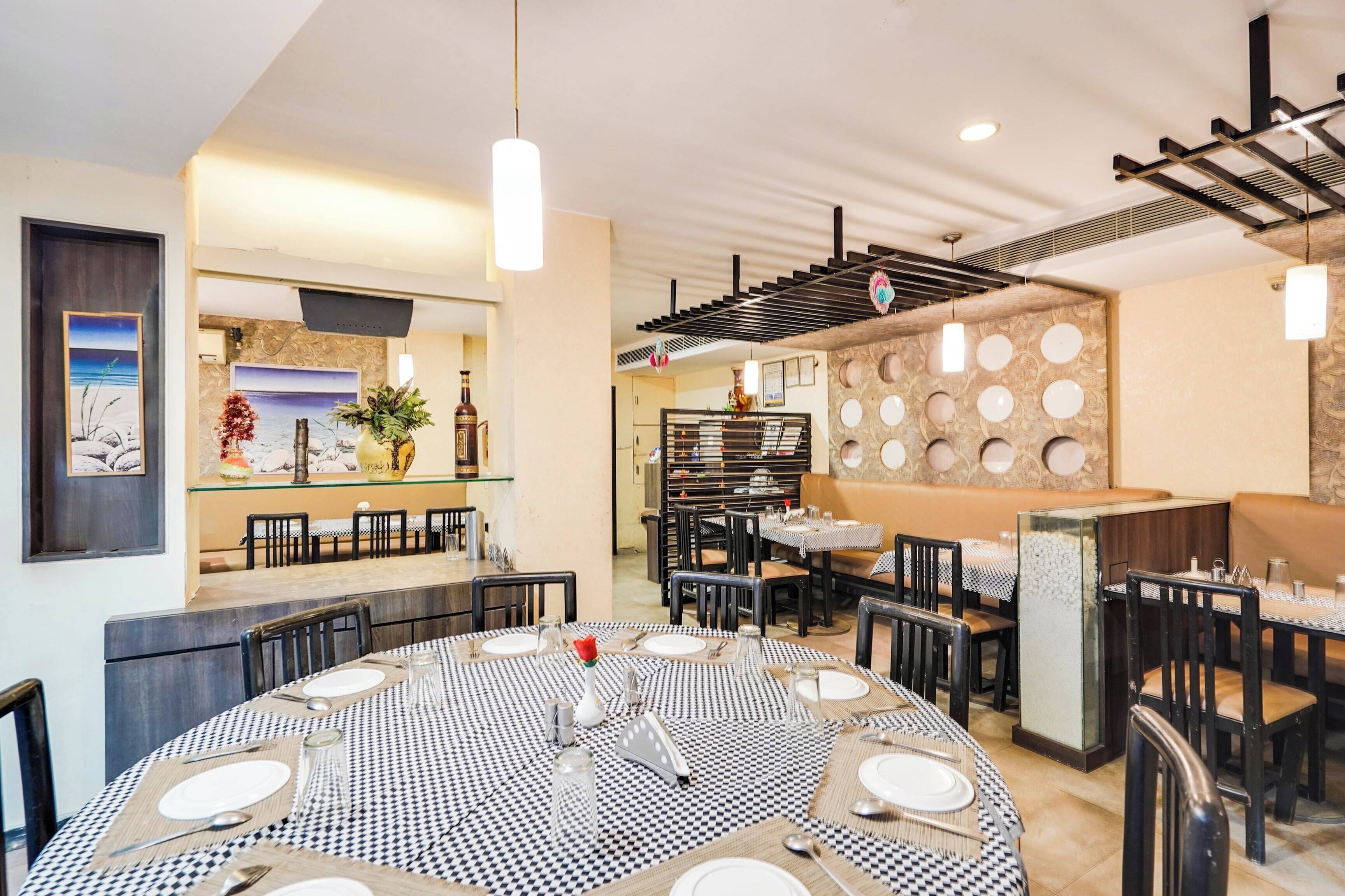 Restaurante com mesas redondas, toalhas xadrez em preto e branco, e diferentes opções de assentos, incluindo cabines e cadeiras.