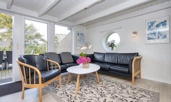 Uma sala de estar moderna com um sofá de couro preto, uma cadeira de madeira, uma mesa de centro branca e um espelho redondo na parede.
