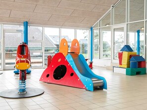 Espaço infantil coberto com escorrega, estruturas de escalada e brinquedo com mola.