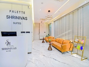 Uma área de recepção de hotel com um balcão branco, um sofá e um expositor com livros.