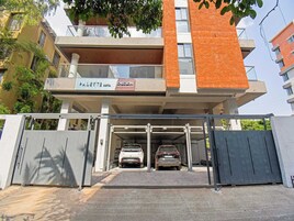 Um edifício de vários andares com entrada fechada por portão, dois carros estacionados no interior e uma varanda visível com um aviso.