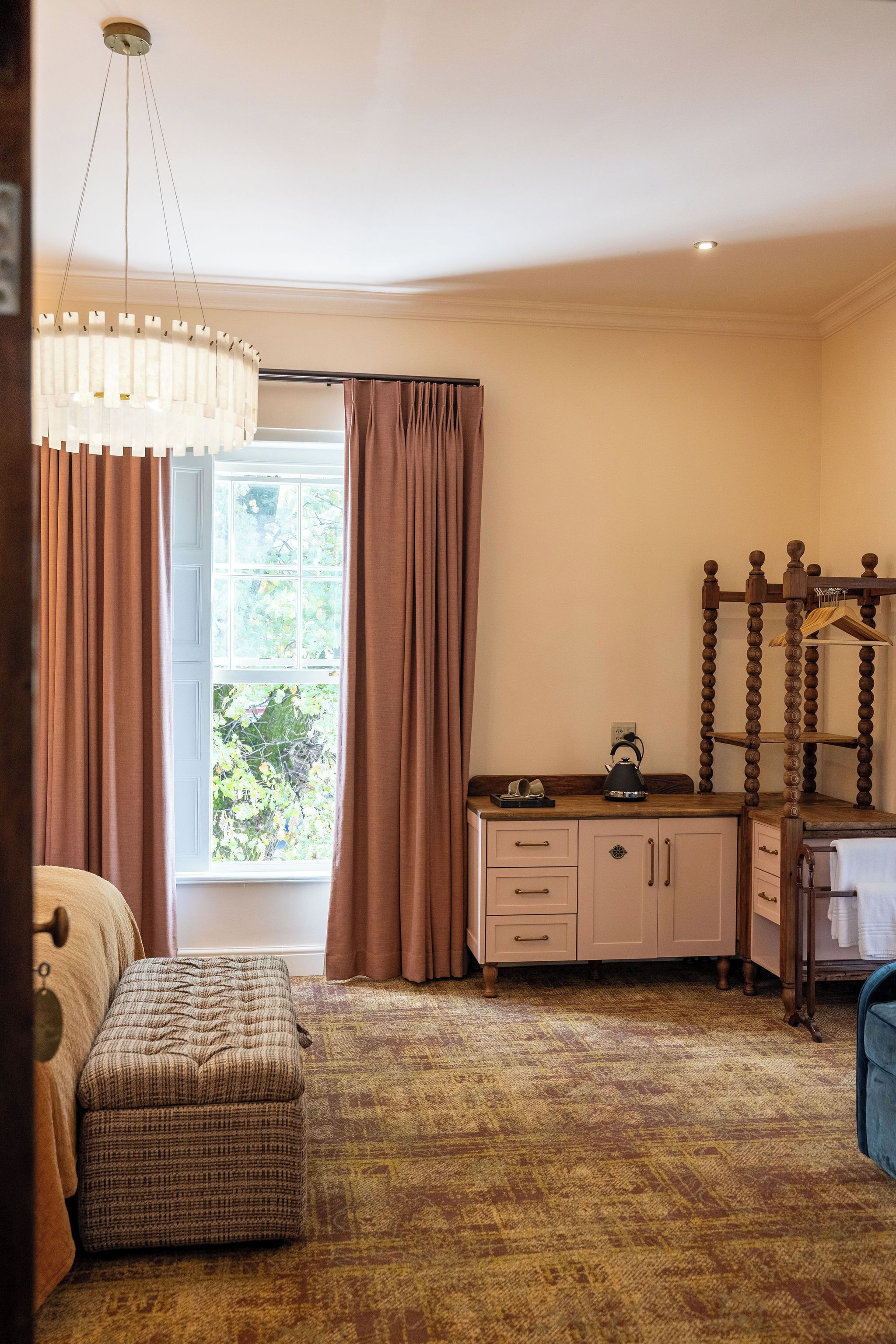Um quarto com cama, cômoda, luminária pendente e janela com cortinas.