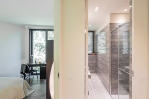 Quarto de hotel moderno com cama, escrivaninha e área de chuveiro.