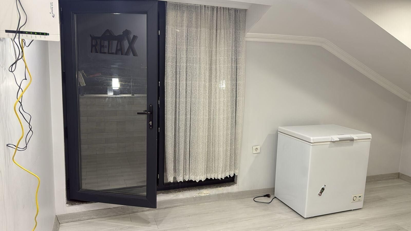 Um quarto com porta deslizante, geladeira branca e cortina.