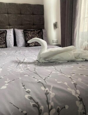 Cama com manta em formato de cisne, cabeceira e almofadas estampadas.