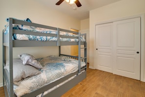 Uma cama beliche com roupa de cama estampada, um ventilador de teto e uma porta branca num quarto com soalho de madeira.