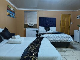 Quarto de hotel com duas camas, uma escrivaninha, uma janela com persianas e uma porta.