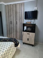 Quarto com cama, guarda-roupa, televisão e um pequeno armário.