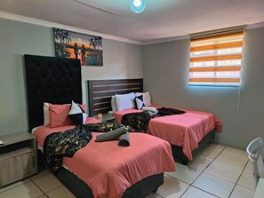 Quarto com duas camas, uma mesa de cabeceira, uma cadeira, janela com persianas e um quadro na parede.