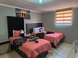 Quarto com duas camas, uma mesa de cabeceira, uma cadeira, janela com persianas e um quadro na parede.