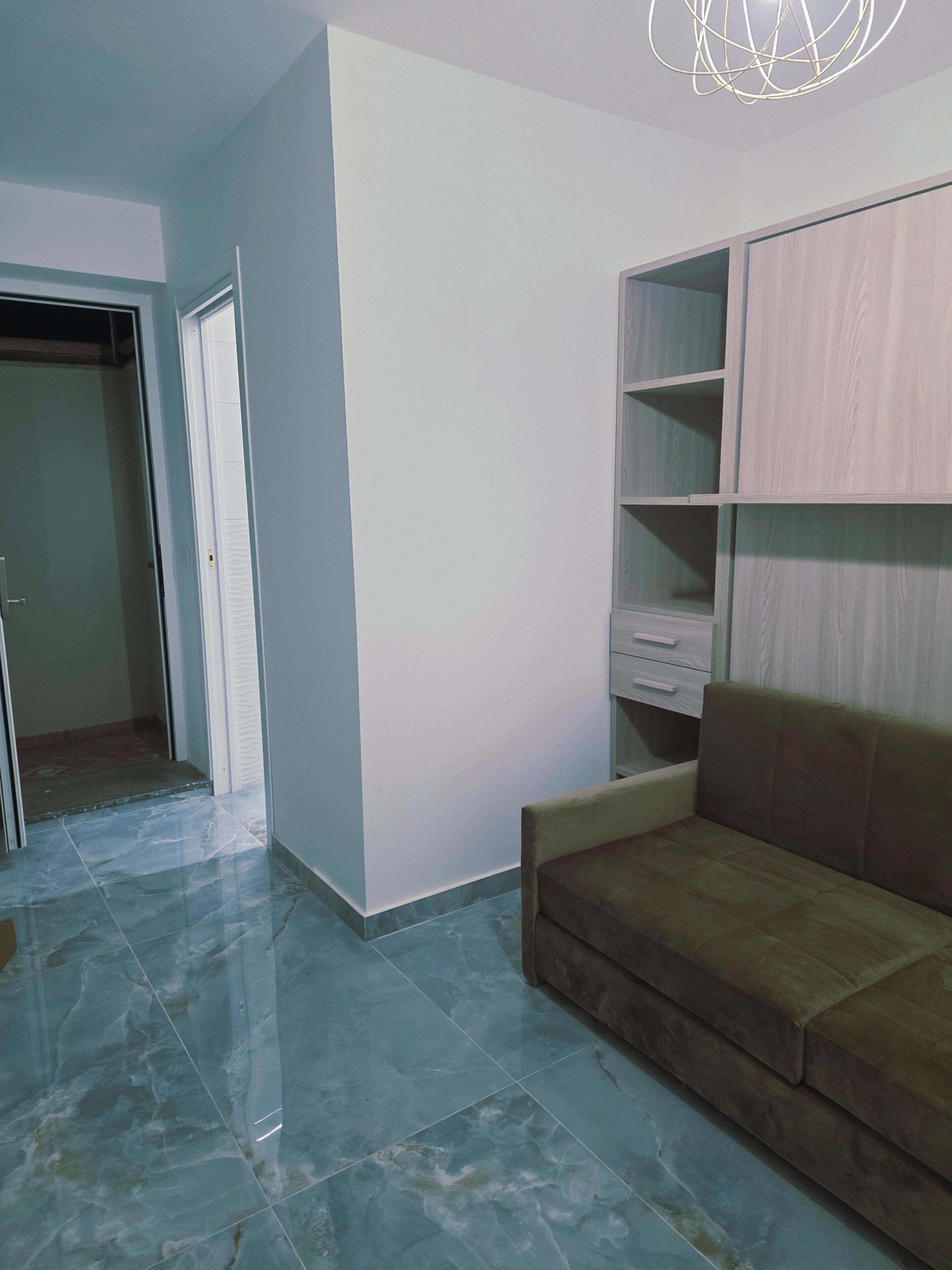 Quarto com sofá marrom, armário de madeira e chão de azulejos.